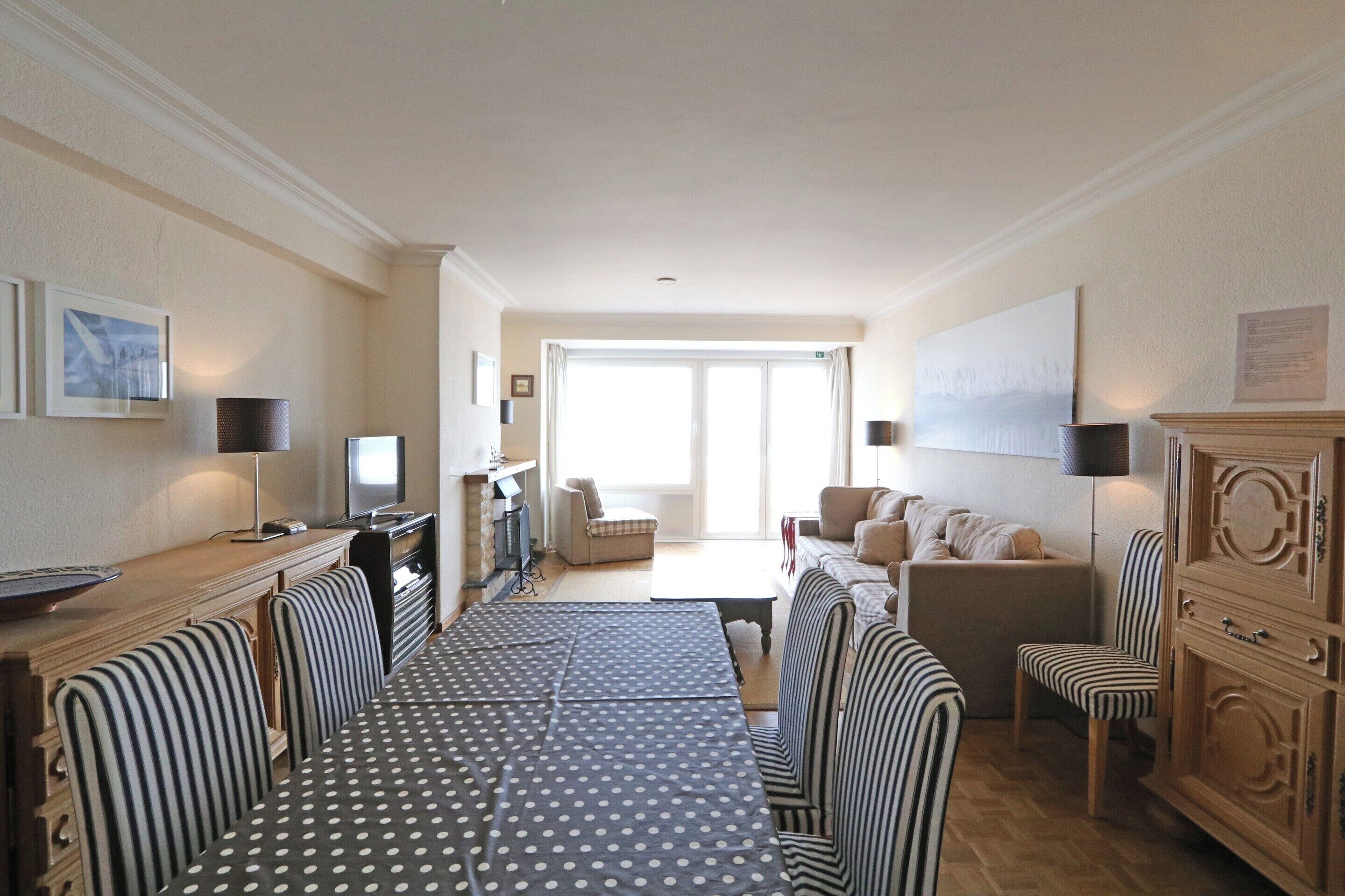 Uma sala de estar com sofá, poltronas, mesa de jantar com cadeiras, televisão e lareira.