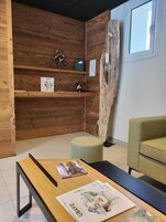 Quarto com paredes de madeira, um banquinho estofado verde, um sofá verde e uma mesa de madeira com uma revista.