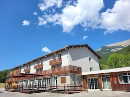 Hotel com vários andares, varandas, fachada de pedra e montanhas ao fundo.