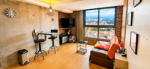 Espaço compacto com cozinha compacta, uma janela ampla vista da cidade, sofá de couro e televisão na parede.