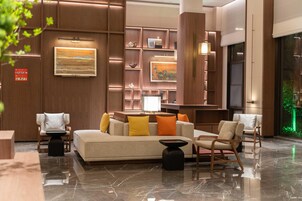 Um saguão moderno com um sofá, cadeiras, uma mesa de centro e uma estante com objetos decorativos.
