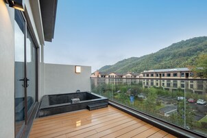 Uma varanda com piso de madeira, uma banheira de hidromassagem e vista para um estacionamento e edifícios ao fundo.