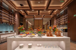 Um lobby de hotel moderno com área de buffet central, painéis de madeira e painel de azulejos.