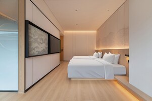 Quarto de hotel moderno com design minimalista, apresentando uma cama grande, televisão de tela plana na parede e um quadro abstrato de grandes dimensões.