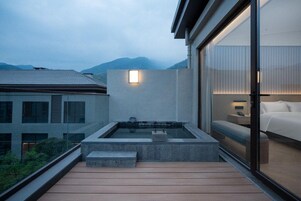 Quarto de hotel moderno com uma grande porta de vidro deslizante, varanda privativa com hidromassagem e vista para montanhas.