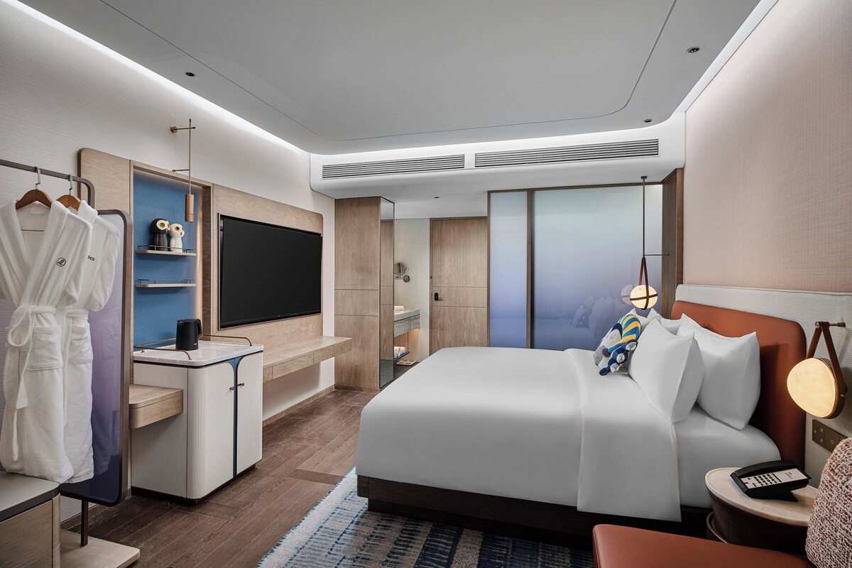 Quarto de hotel moderno com uma cama grande, uma escrivaninha com TV de tela plana, porta-robes e um espelho.