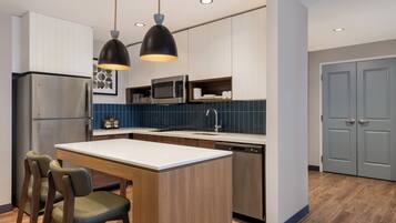 Cozinha moderna com ilha central, eletrodomésticos de aço inoxidável e iluminação pendente.