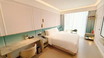 Quarto de hotel com cama, escrivaninha, cadeira, mesa pequena, espelho e guarda-roupa.