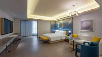 Quarto de hotel moderno com cama, sofá, mesa pequena, banquinho e televisão.