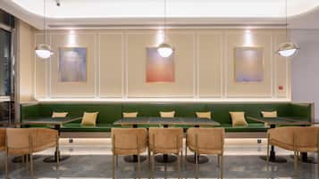 Restaurante moderno com assentos acolchoados em verde, uma mesa comprida e luminárias pendentes.