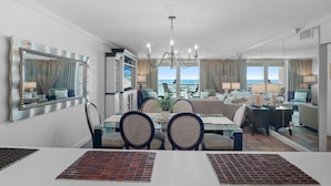 Uma sala de jantar espaçosa com uma mesa grande e cadeiras, um lustre e vista para o oceano.