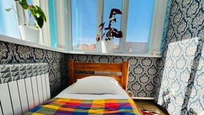 Uma cama com um edredom colorido xadrez, uma toalha branca e uma janela com vista para as montanhas, além de papel de parede estampado.