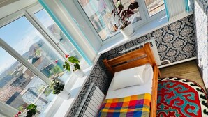 Quarto com cama, radiador, janela com vista para montanhas e papel de parede estampado.