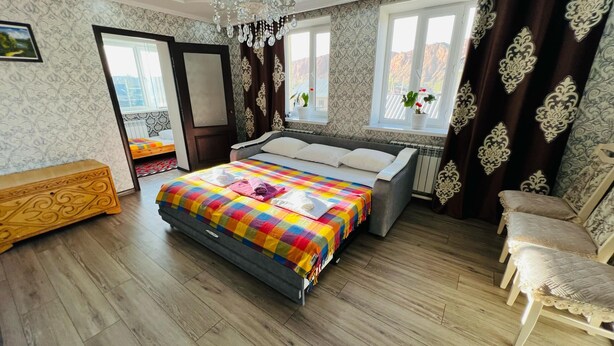 Quarto de hotel com uma cama grande, cómoda de madeira, uma cadeira e janela com cortinas.