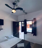 Quarto com cama, ventilador de teto, janela com cortinas e vista para o exterior.