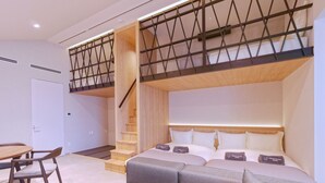 Quarto de hotel moderno com cama mezanina, sofá, área de jantar e escada.