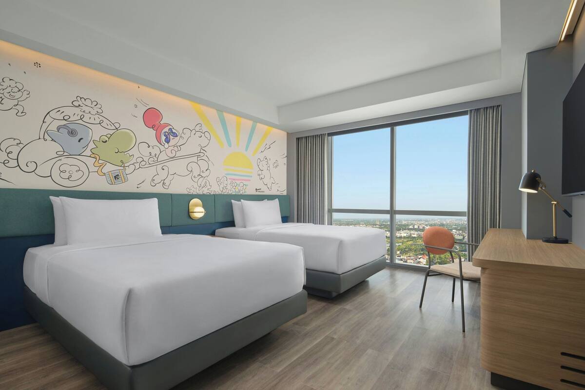 Quarto de hotel com duas camas, uma escrivaninha e vista para a cidade.