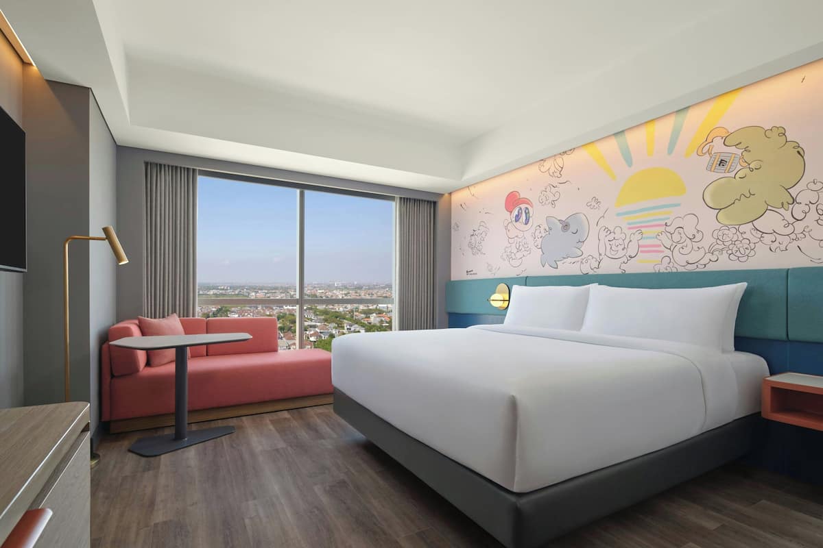 Quarto de hotel moderno com uma cama grande, um sofá, uma mesinha e vista para a cidade.