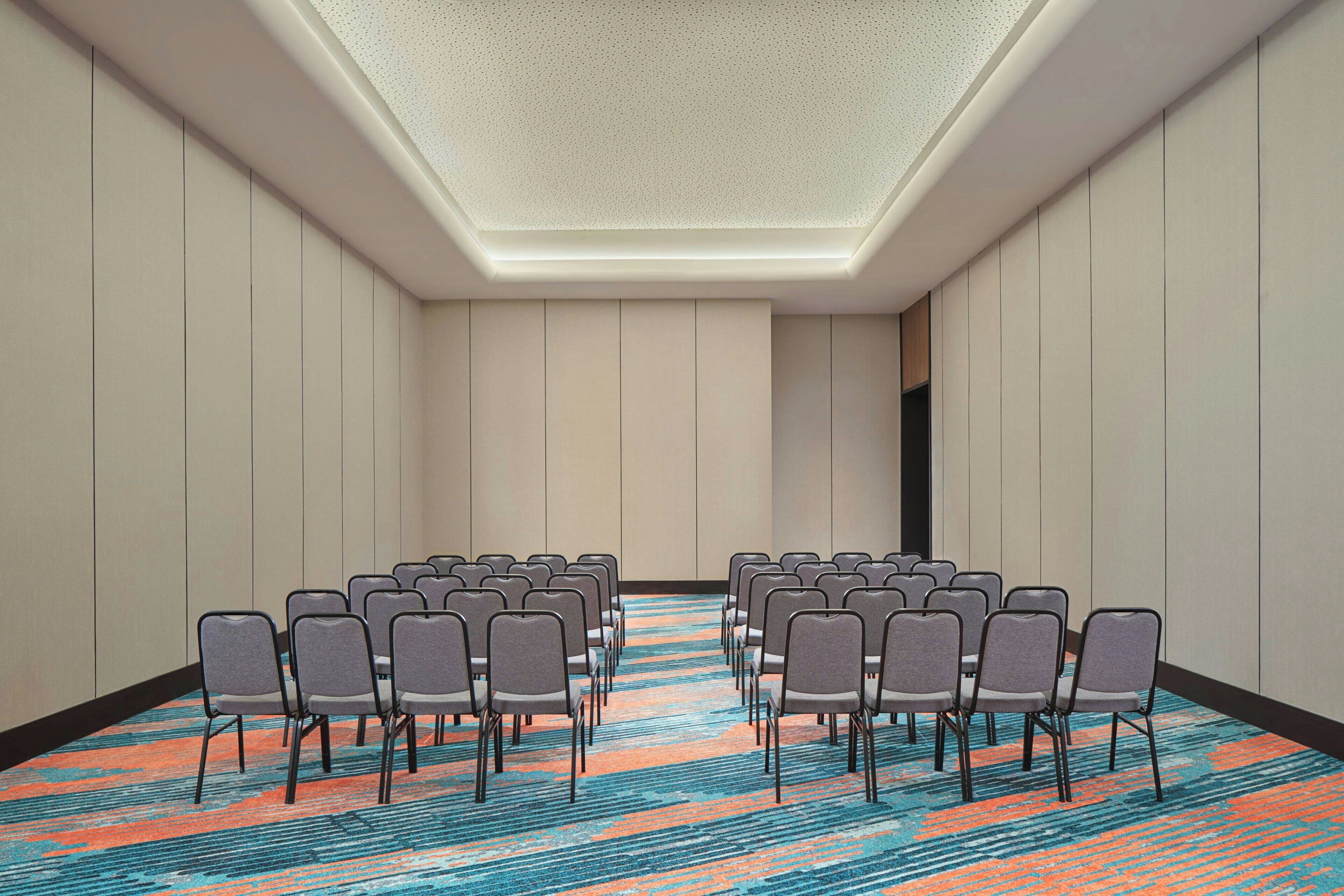Uma sala de conferências com fileiras de cadeiras, um tapete estampado e um lustre no teto.
