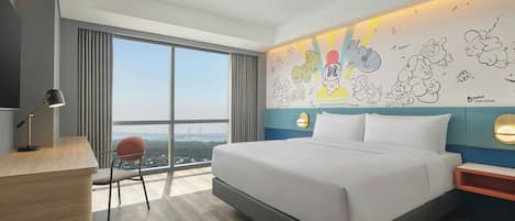 Quarto de hotel moderno com uma cama grande, uma escrivaninha, uma cadeira e vista da cidade através de janelas do chão ao teto.