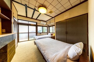 Quarto de hotel com duas camas, um guarda-roupa espaçoso, uma escrivaninha com luminária e uma janela ampla que oferece uma vista.