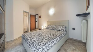 Um quarto com cama, mesa de cabeceira, abajur, porta e radiador.
