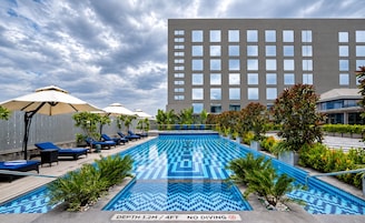 Piscina com espreguiçadeiras e guarda-sóis, cercada por vegetação, com um edifício ao fundo.