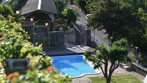 Área residencial com piscina, portão fechado e casa com telhado inclinado.