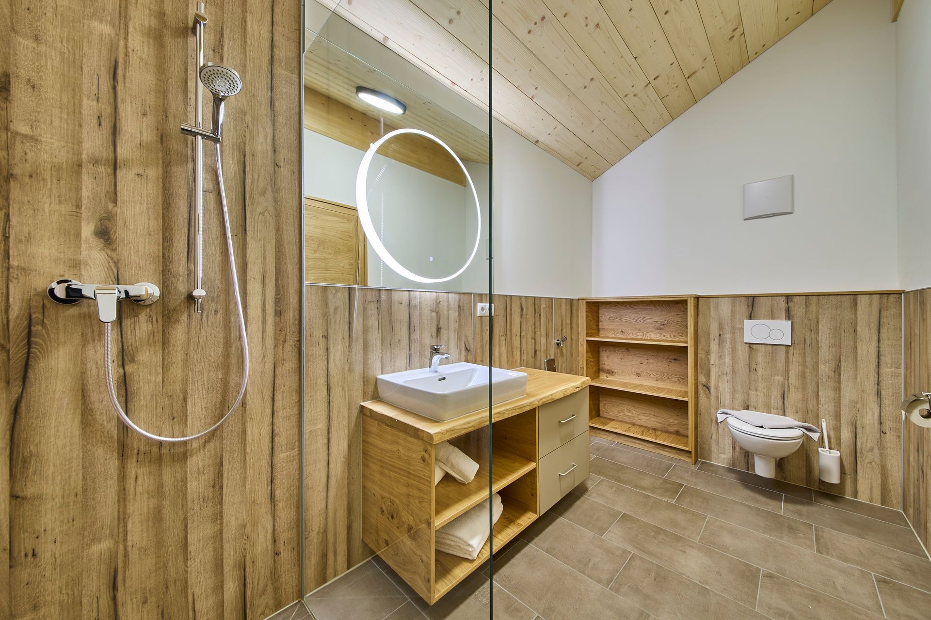 Casa de banho moderna com painéis de madeira, cabine de duche envidraçada, toucador com lavatório e sanita.