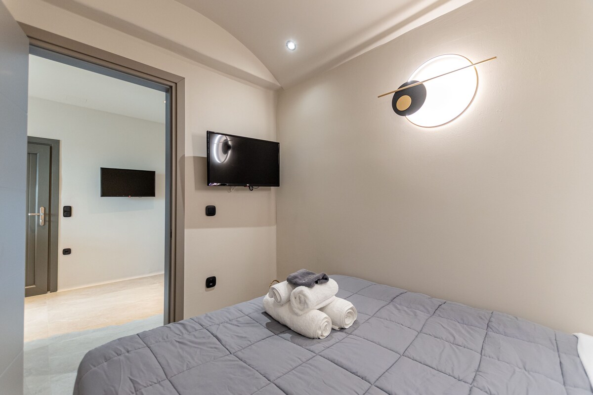 Quarto com cama, TV de tela plana presa na parede e luminária fixada na parede.