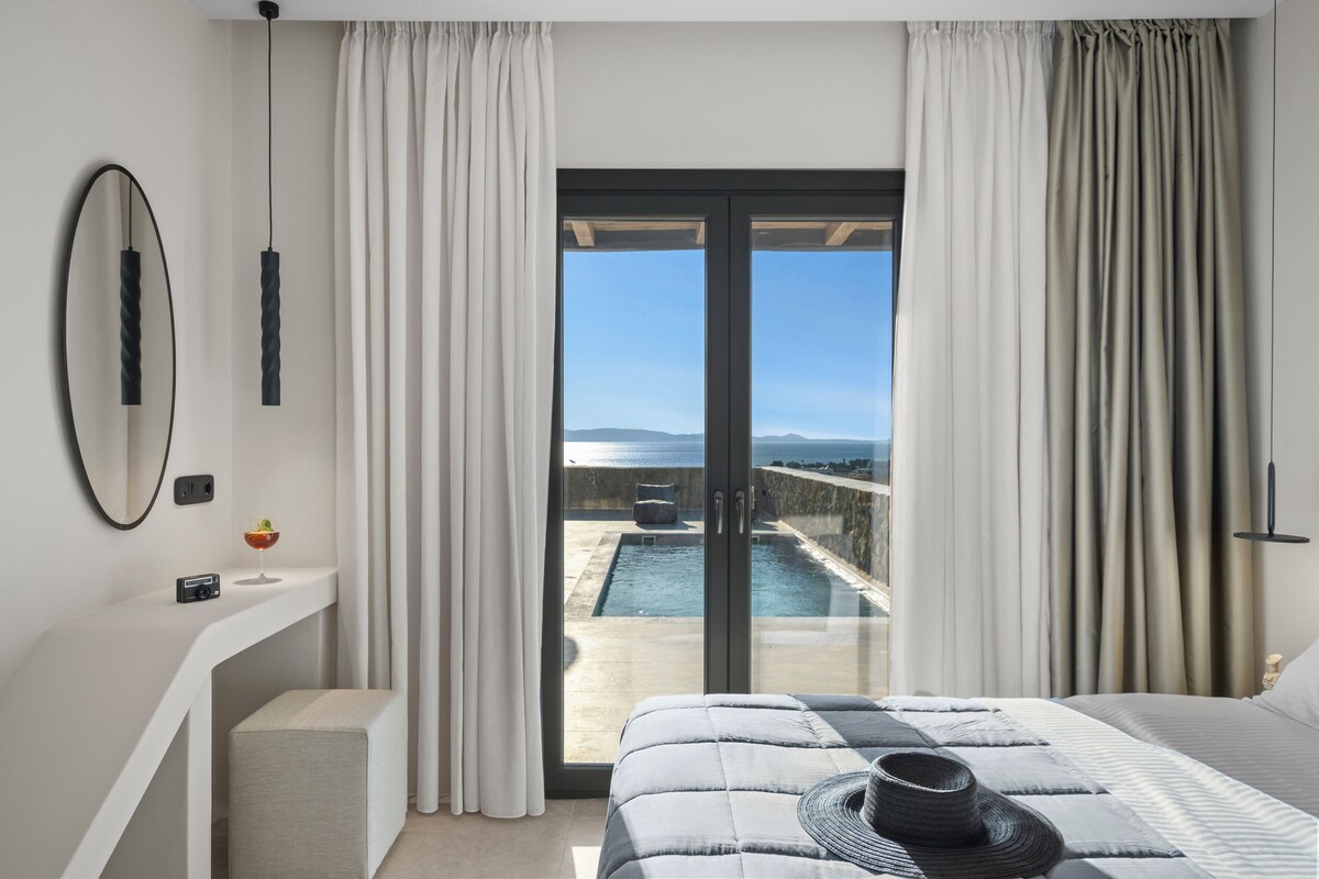 Quarto de hotel moderno com uma cama grande, uma mesinha de cabeceira com rádio, vista para uma piscina ao ar livre e uma varanda com cortinas.
