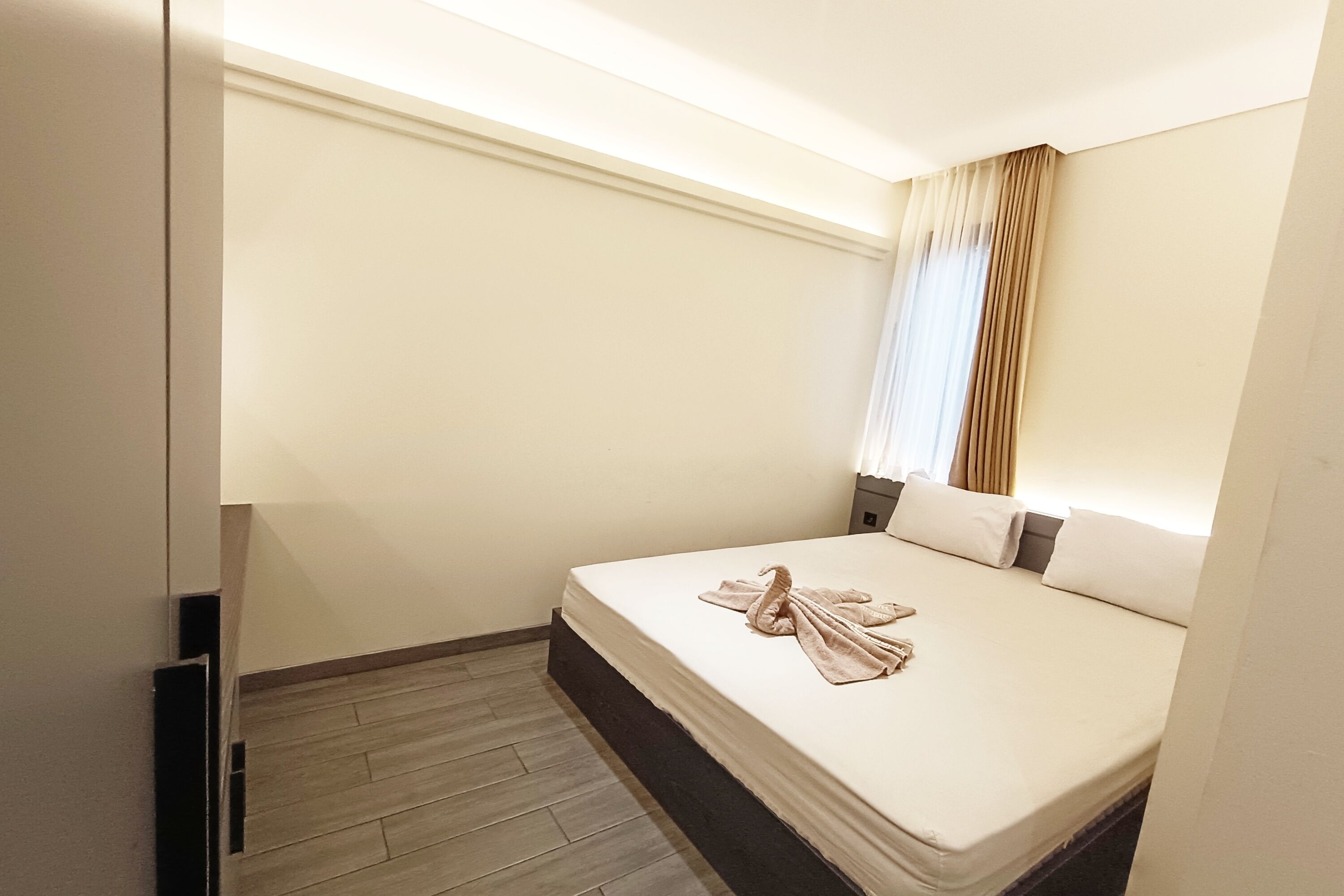 Quarto de hotel com cama, mesa de cabeceira e janela com cortinas.