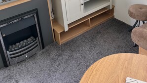 Uma sala de estar moderna com televisão de tela plana em um suporte de madeira, lareira, janela com persianas e um pequeno vaso com planta.