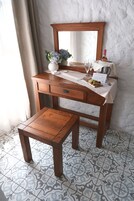 Uma toucador de madeira com espelho, uma pequena mesa e um vaso com flores.