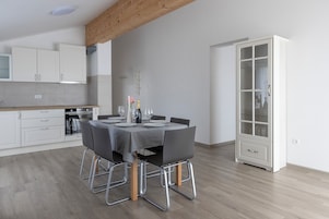 Uma cozinha moderna com armários brancos, uma mesa de jantar posta para quatro pessoas e um armário grande branco com portas de vidro.