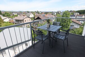 Uma varanda com mesa e cadeiras, com vista para uma área residencial com casas e vegetação.