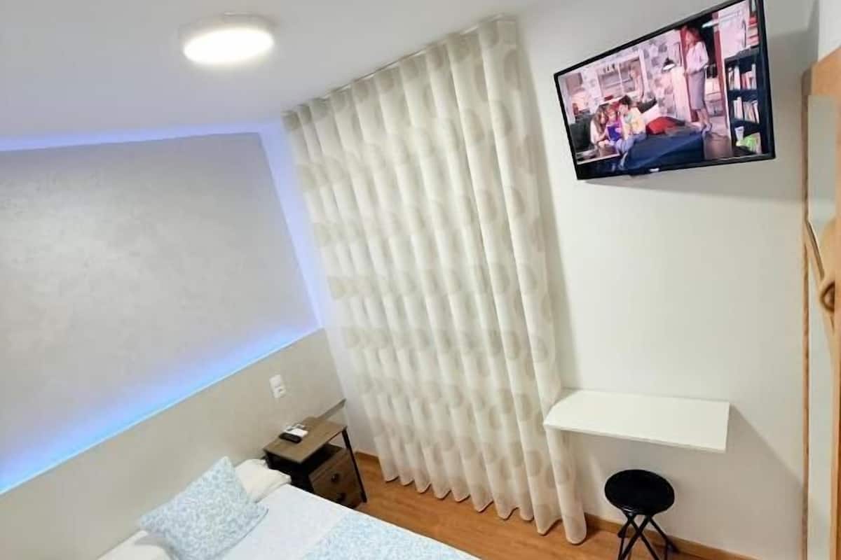 Quarto moderno com cama, escrivaninha, cadeira e televisão na parede.
