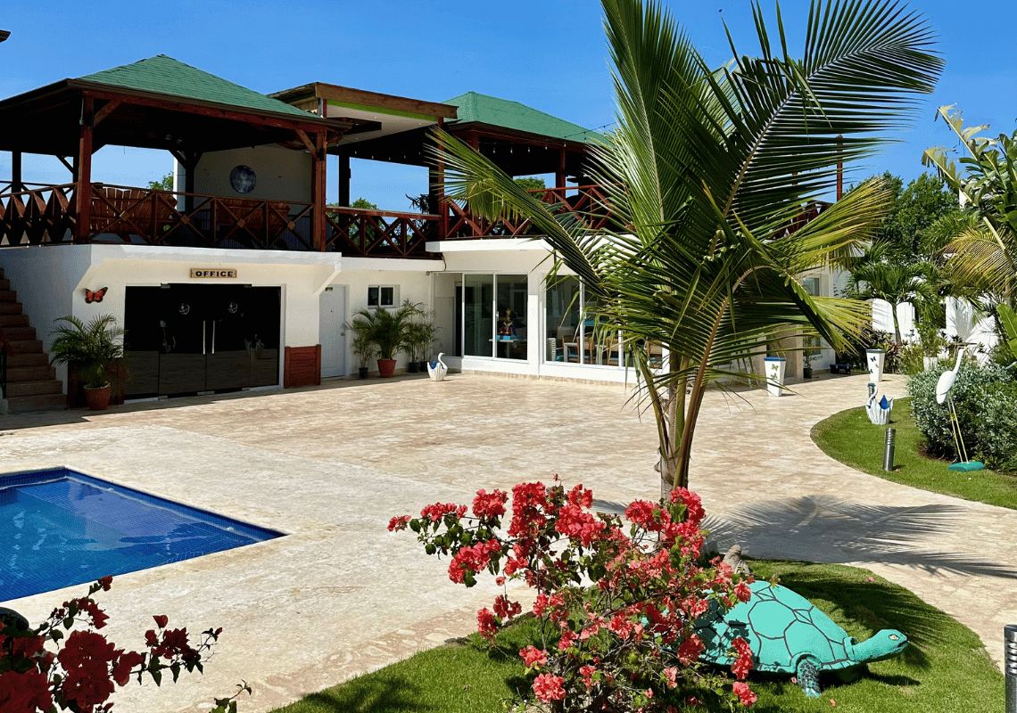 Um hotel com piscina, área externa coberta e jardim com escultura de tartaruga.