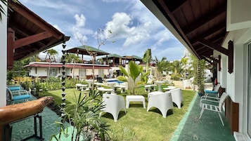 Pátio de hotel com área de estar externa, piscina e espaço coberto com vista para os edifícios ao redor.