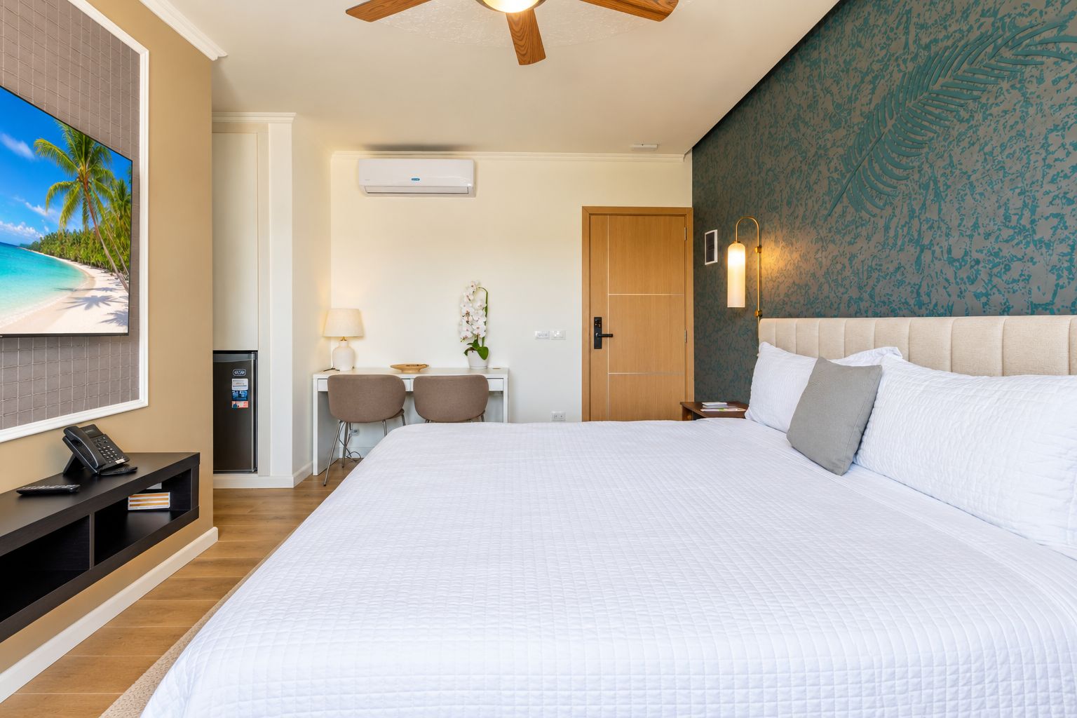 Quarto de hotel com uma cama grande, uma escrivaninha com abajur, televisão e porta.