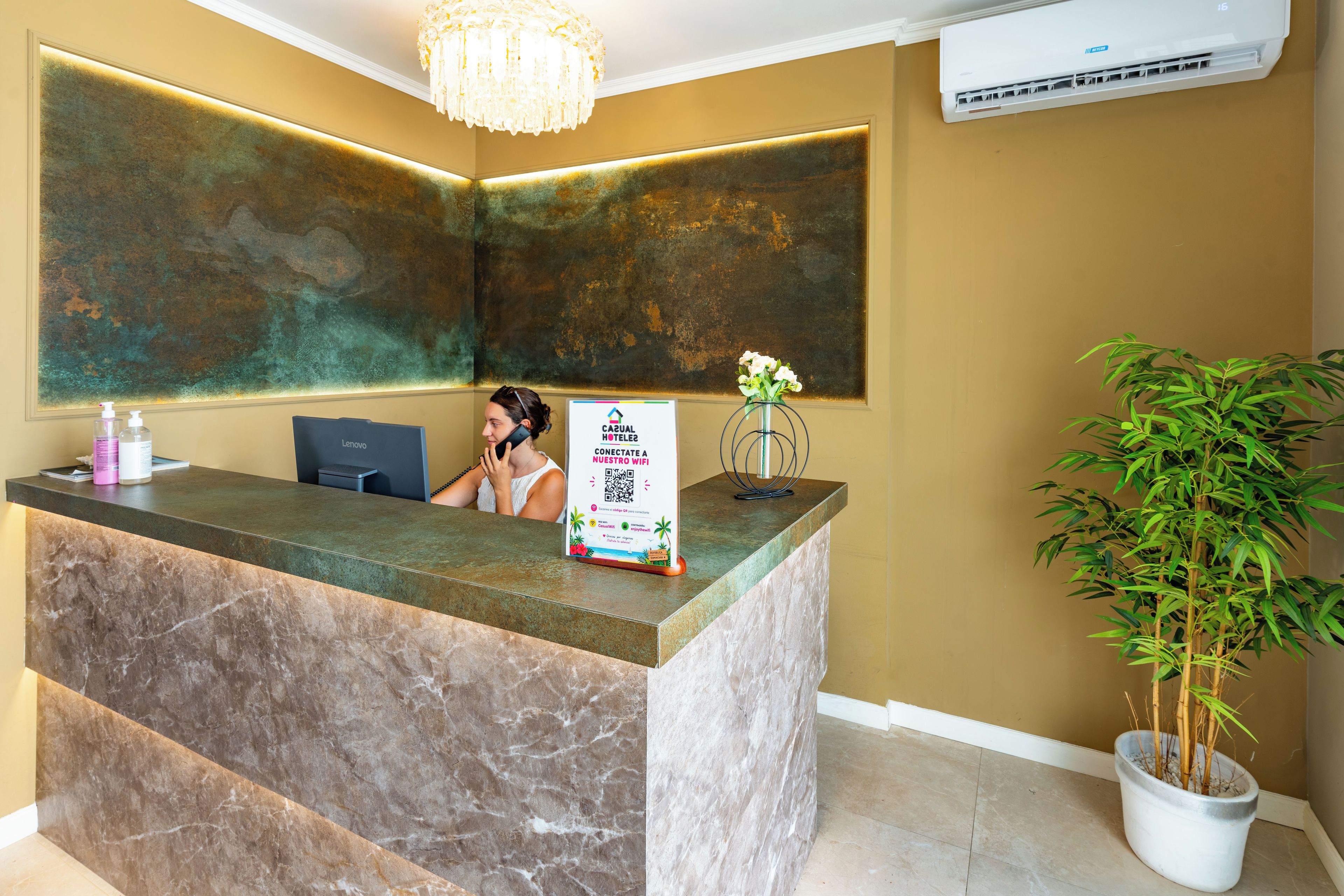 Balcão de recepção de hotel com bancada de mármore, placa oferecendo Wi-Fi gratuito e um vaso de planta.