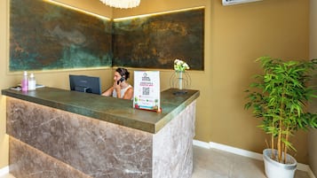 Balcão de recepção de hotel com bancada de mármore, placa oferecendo Wi-Fi gratuito e um vaso de planta.