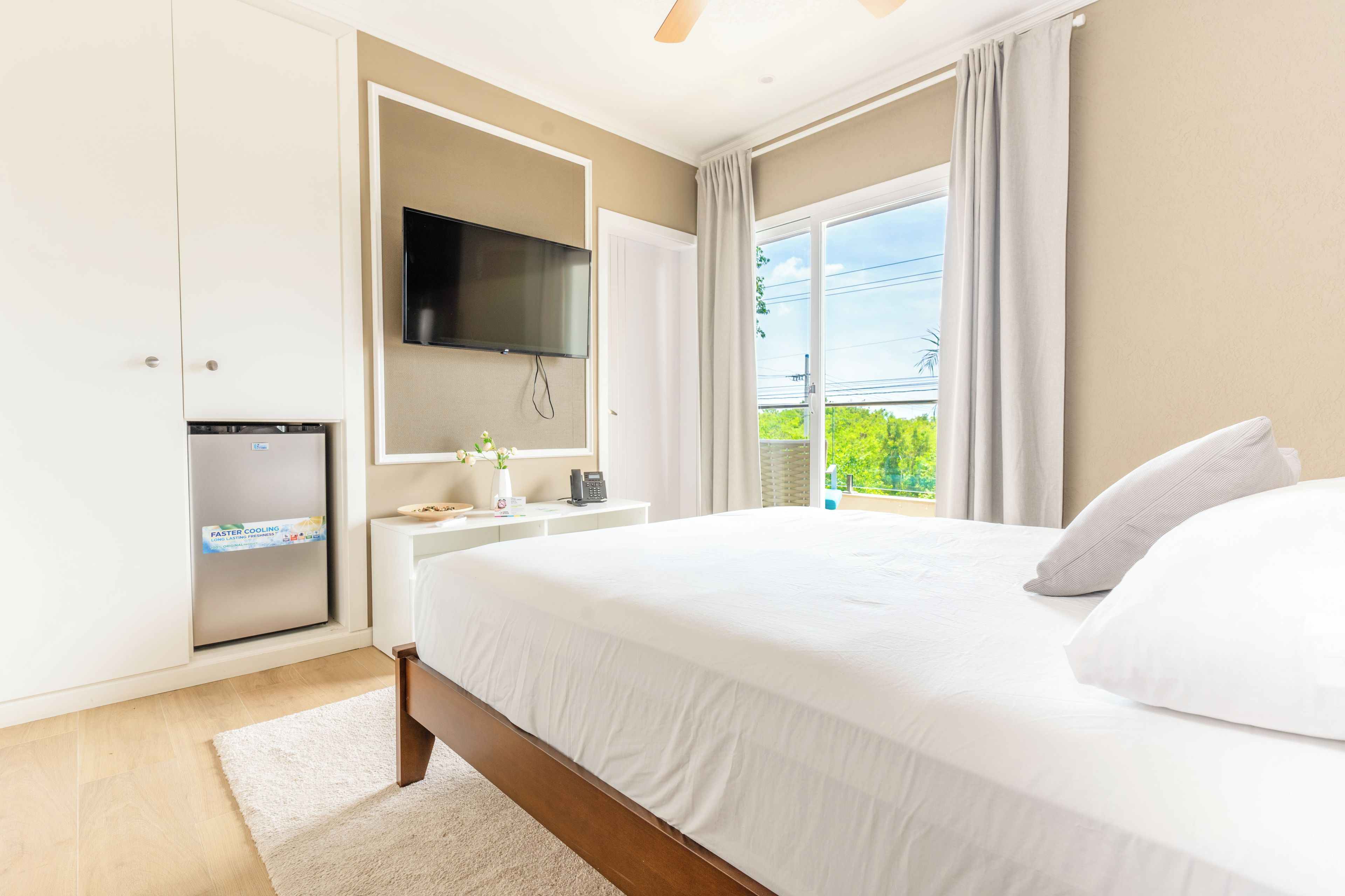 Quarto de hotel com cama, televisão, mini-frigorífico, escrivaninha com telefone e janela com cortinas.