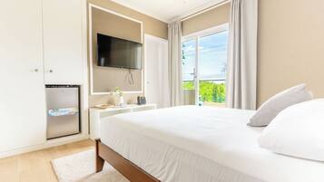 Quarto de hotel com cama, televisão, mini-frigorífico, escrivaninha com telefone e janela com cortinas.