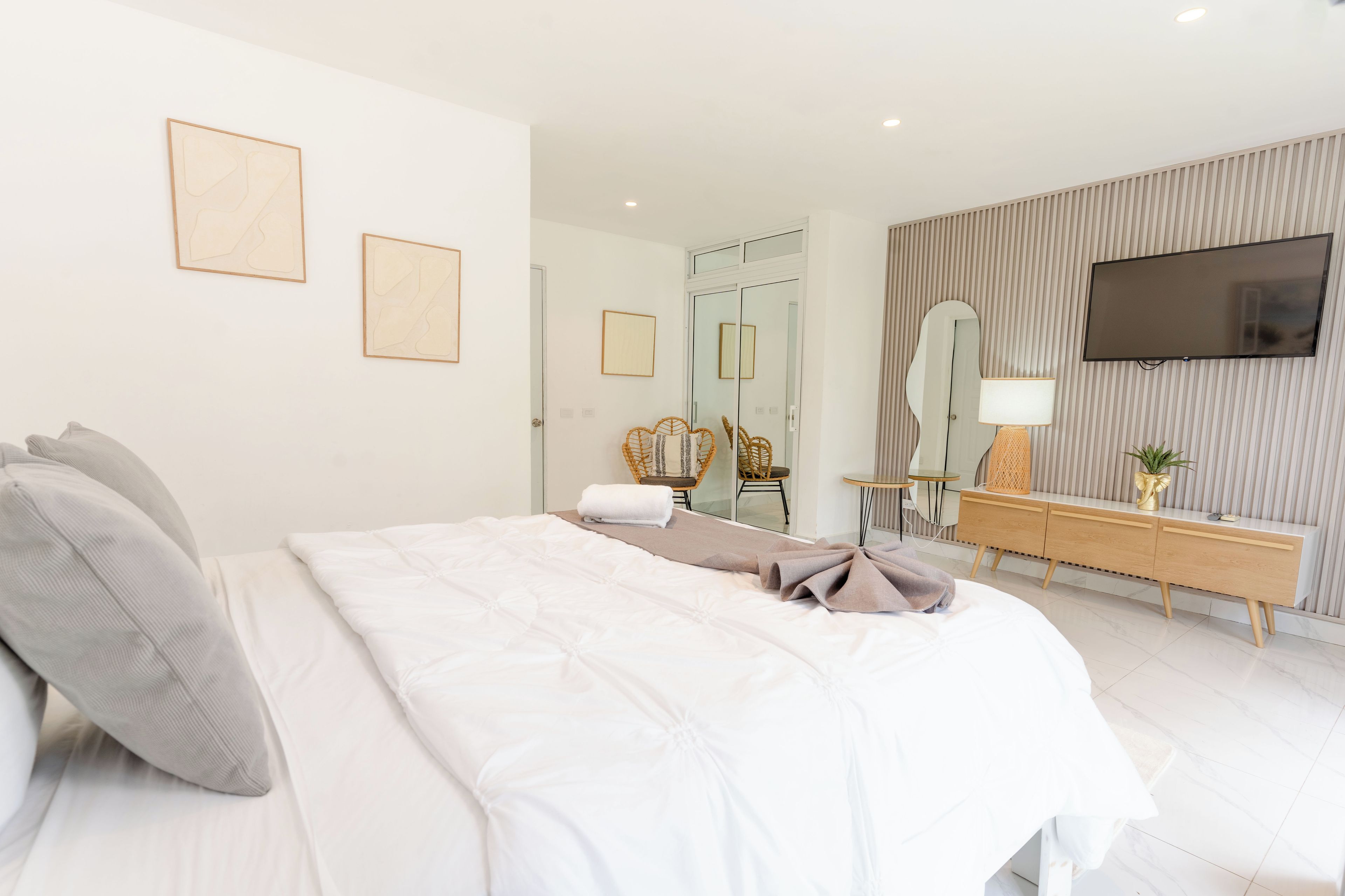 Quarto de hotel moderno com uma cama grande, mesa de cabeceira, televisão, espelho e guarda-roupa.