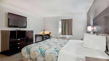 Quarto de hotel com cama, escrivaninha, televisão e janela com cortinas.