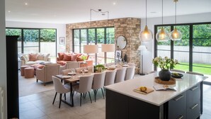 Cozinha moderna com ilha central, área de jantar com cadeiras e sala de estar com sofás e mesa de centro.