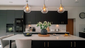 Cozinha moderna com armários escuros, uma ilha branca e três luminárias pendentes.