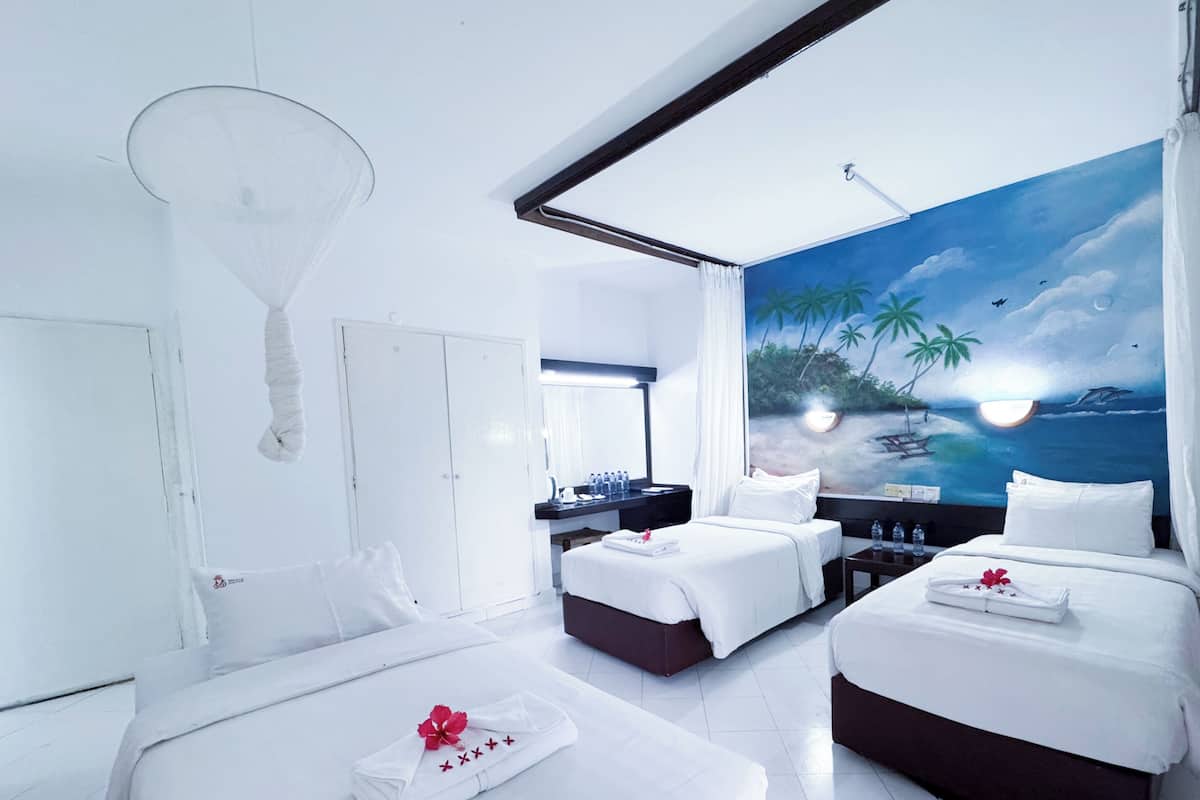 Quarto de hotel com duas camas, uma janela grande, um mural de praia e um ventilador de teto.