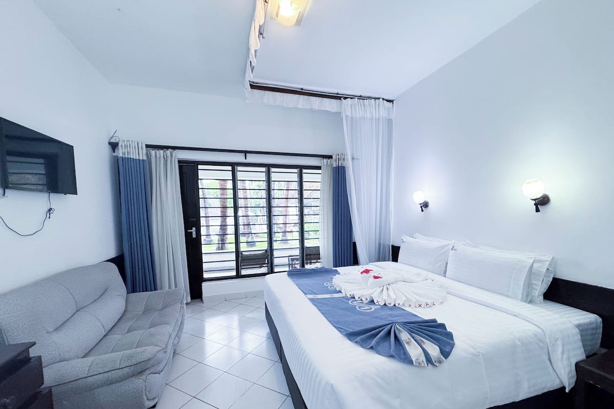 Quarto de hotel com cama, sofá, televisão e porta de vidro deslizante para o exterior.